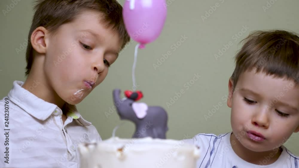 Two boys lick a cake cream. Two boys dressed in white eating birthday ...