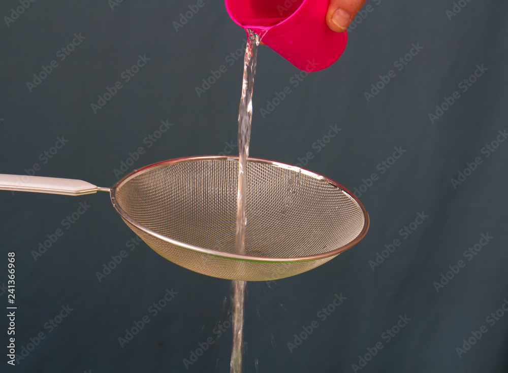 Water poured through a sieve from a pink mag isolated on a clear ...