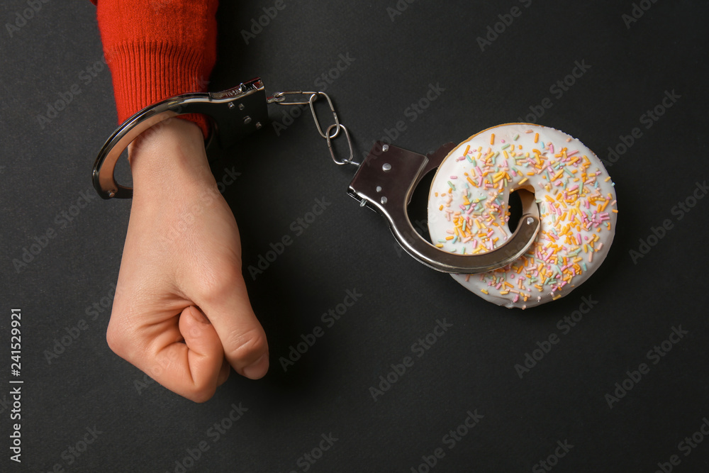 Woman handcuffed to tasty doughnut on dark background. Concept of ...