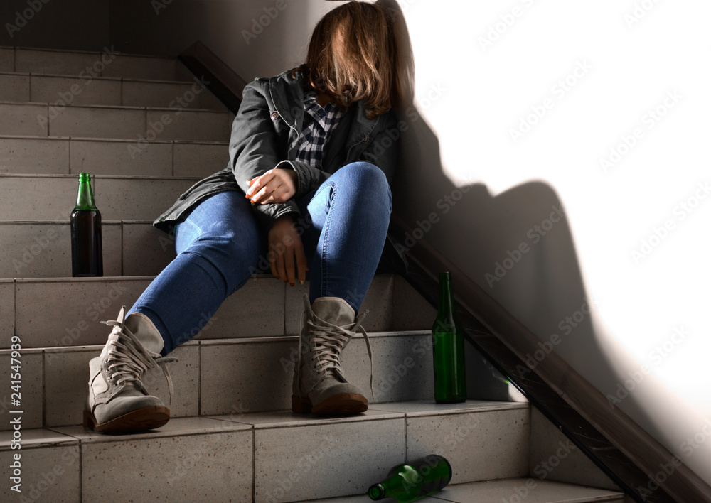 Unconscious young woman with empty bottles sitting on stairs. Concept ...