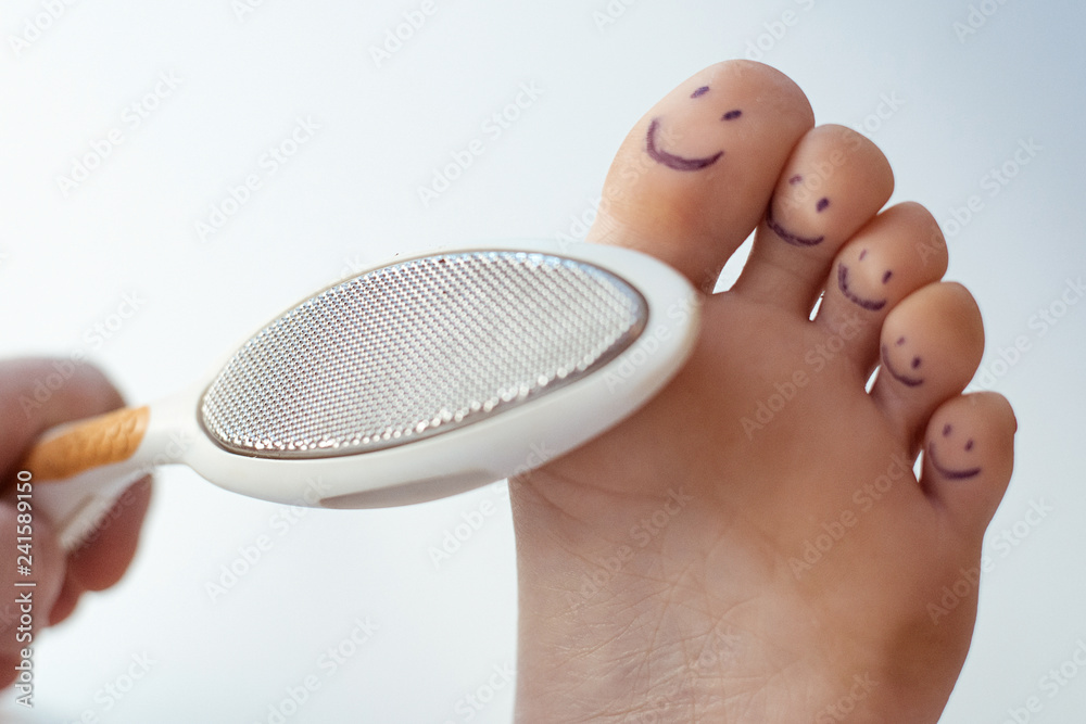 Female toes with painted smileys and a pedicure grater. Foot care ...