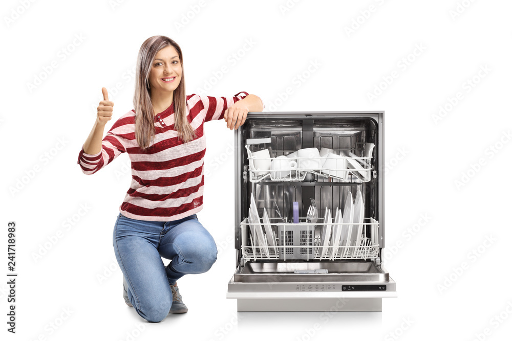 Beautiful young woman kneeling next to an open dishwasher and giving ...