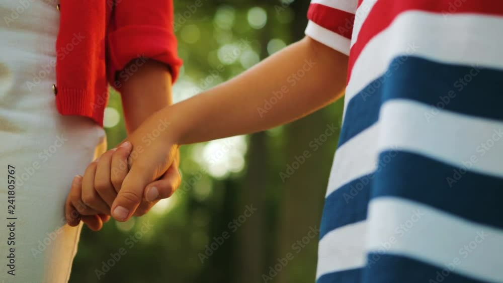 Close up of kids taking each other hands on the green trees blurred ...