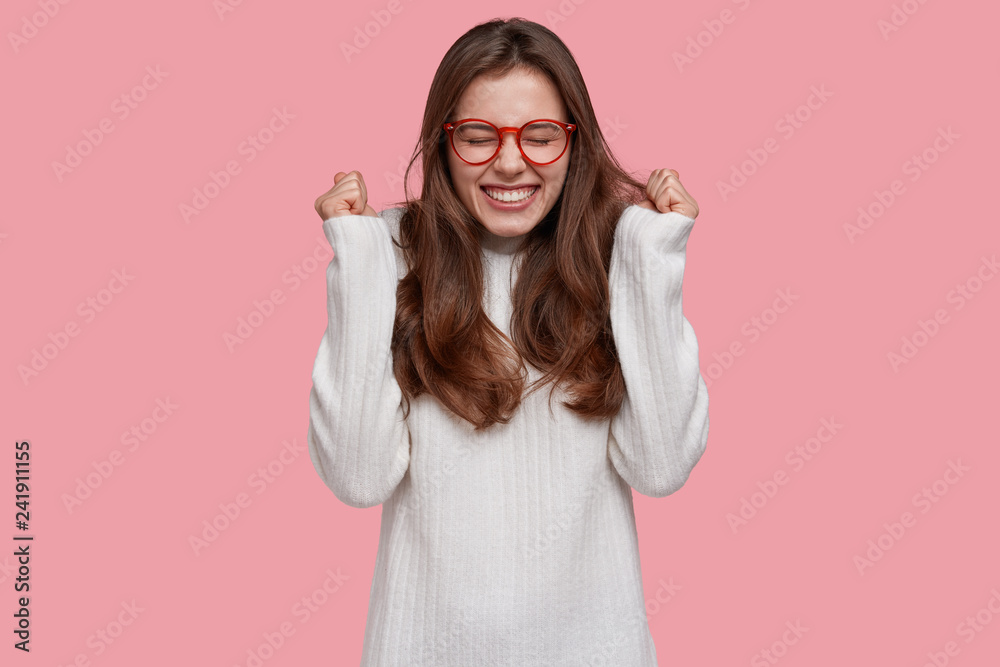 Joful triumphing young woman clenches fists in victory gesture, smiles ...