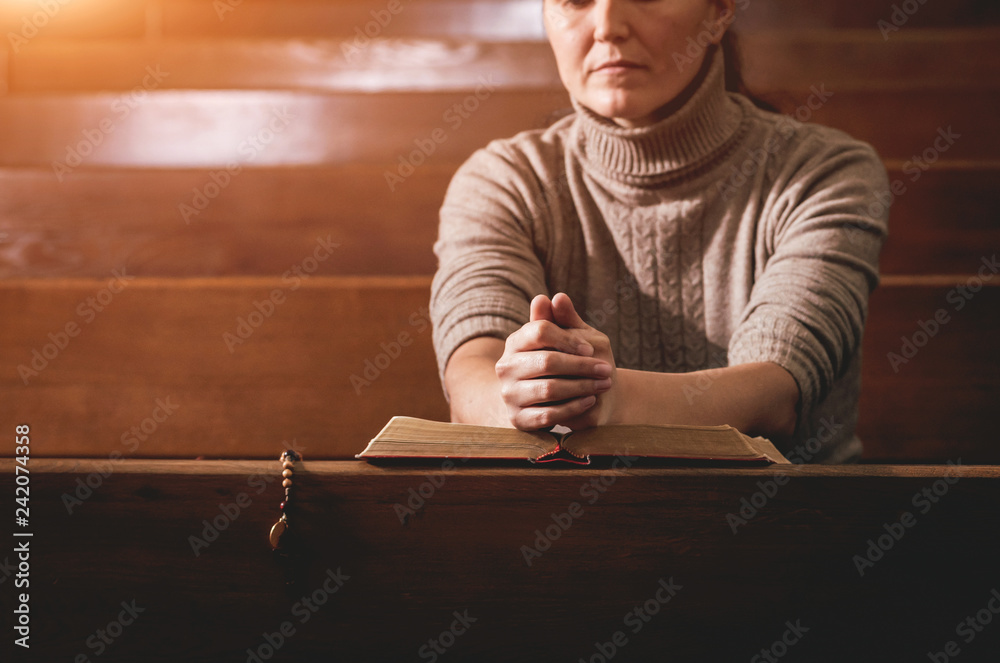 Christian woman praying in church. Hands crossed and Holy Bible on ...
