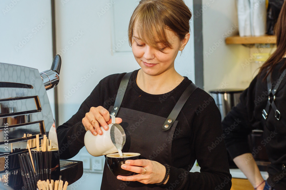 Young female barista in black uniform pouring milk while making ...