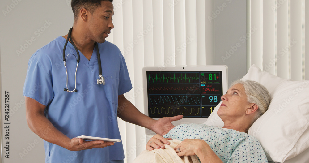 Portrait of male black nurse using tablet computer while attending ill ...
