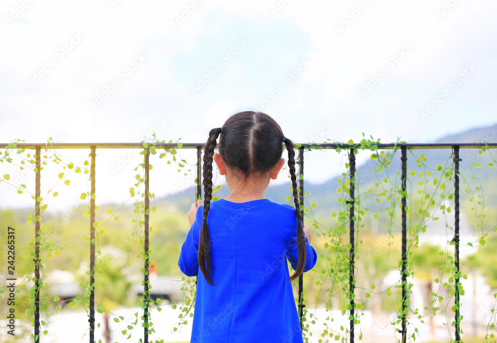 Back view of little girl standing at balcony bars and looking out to ...