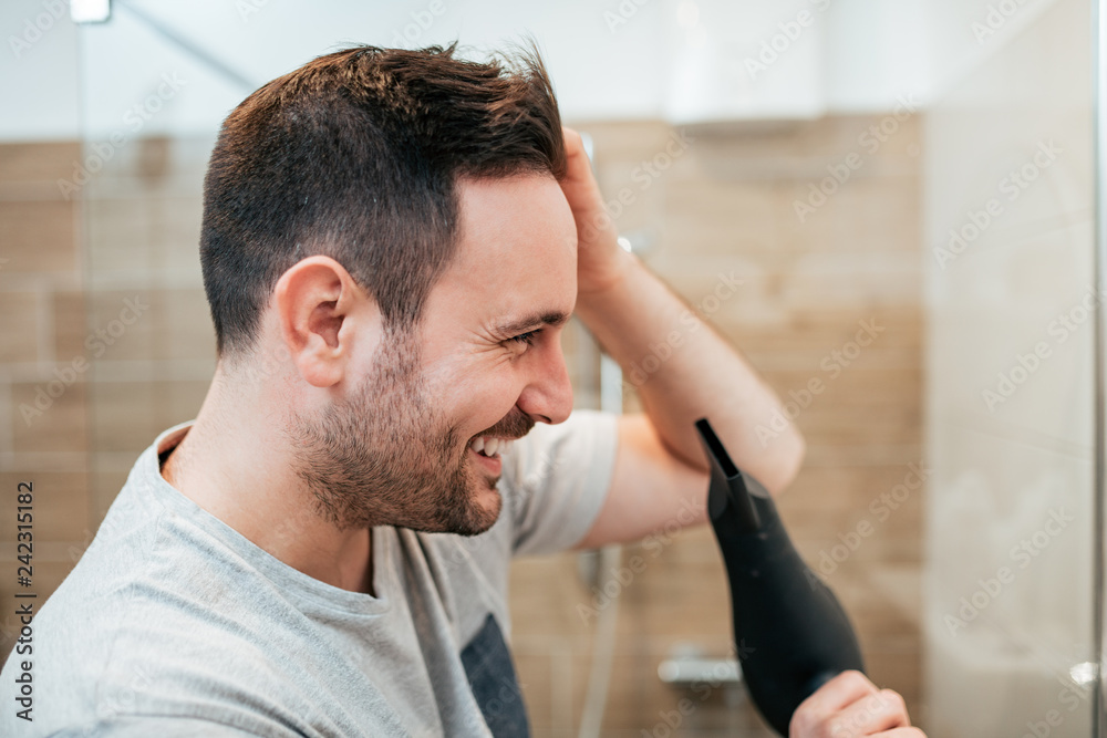 Smiling handsome man blow dry his hair in bathroom. Close-up, side view ...
