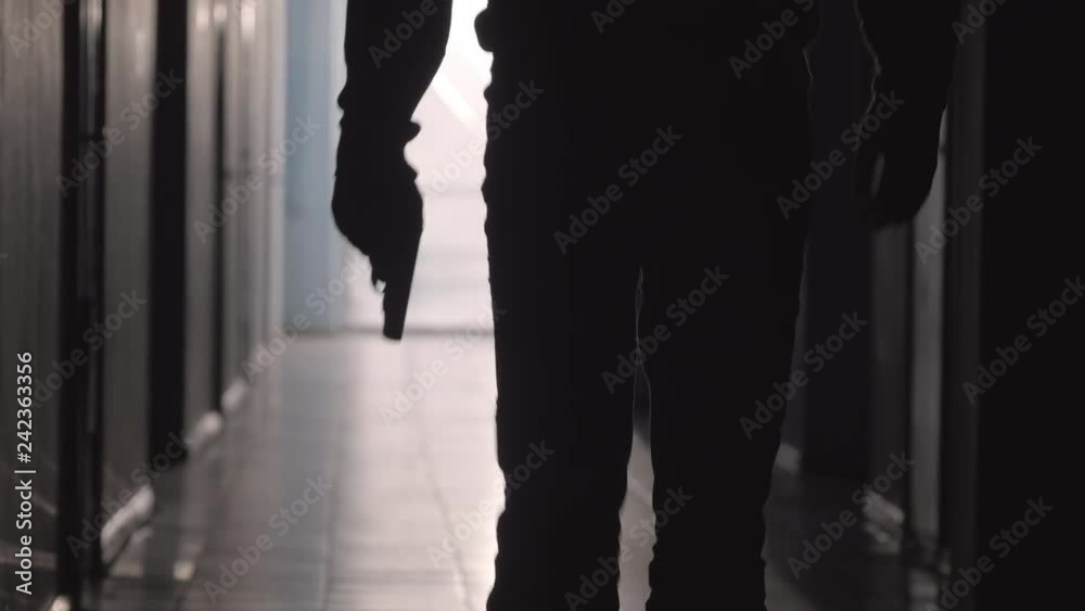 Tilt up shot of silhouette of unrecognizable man walking with handgun ...