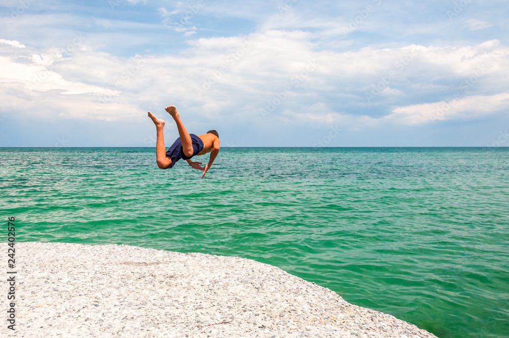 Young boy jumping into the Aegean sea waters from rocky beach in ...