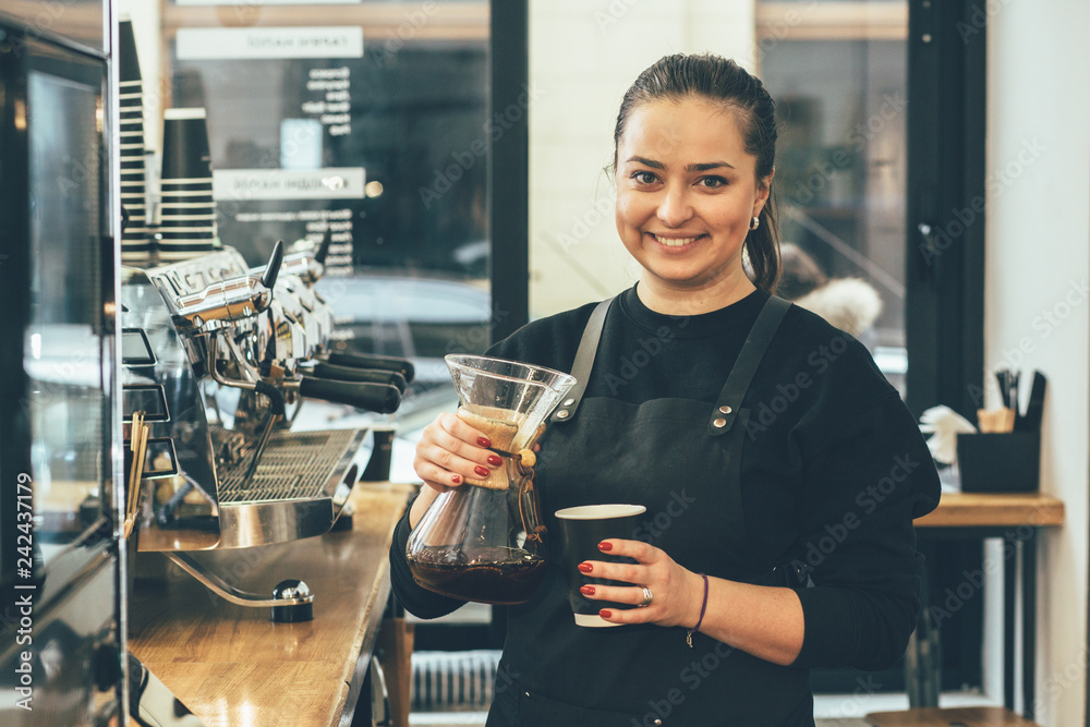 Positive friendly smiling female barista in black uniform preparing ...