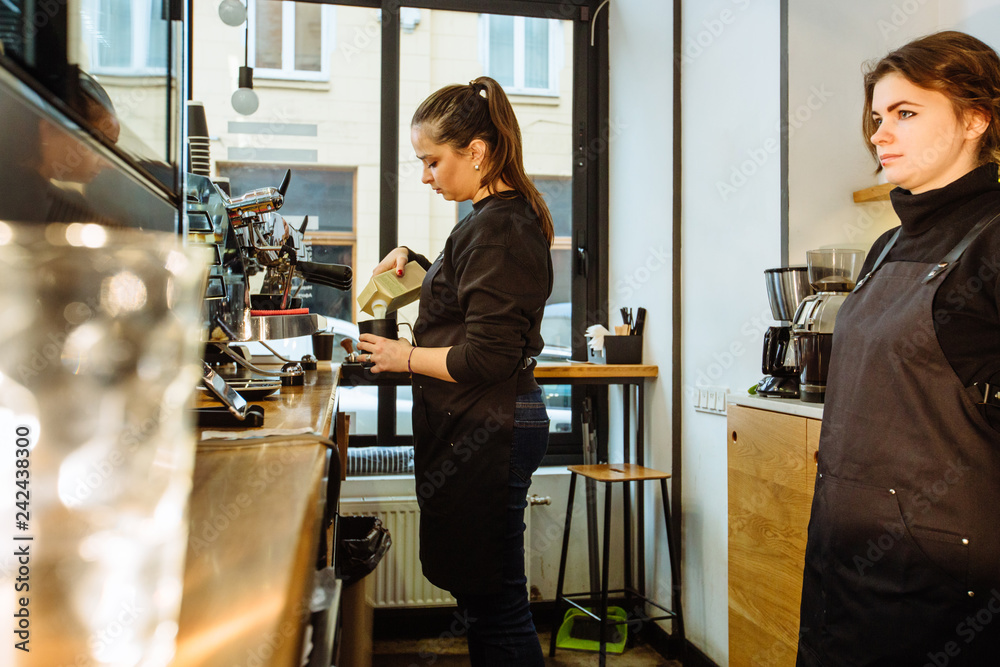 Caucasian female barista in black uniform pouring milk for cappuccino ...