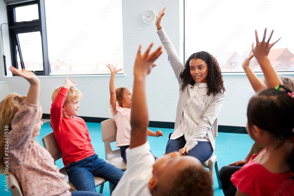 A class of infant school children sitting on chairs in a circle in the ...