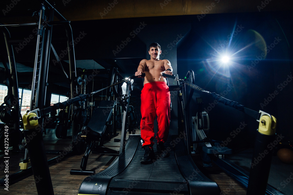 Shirtless young male holding ropes and running on treadmill while ...