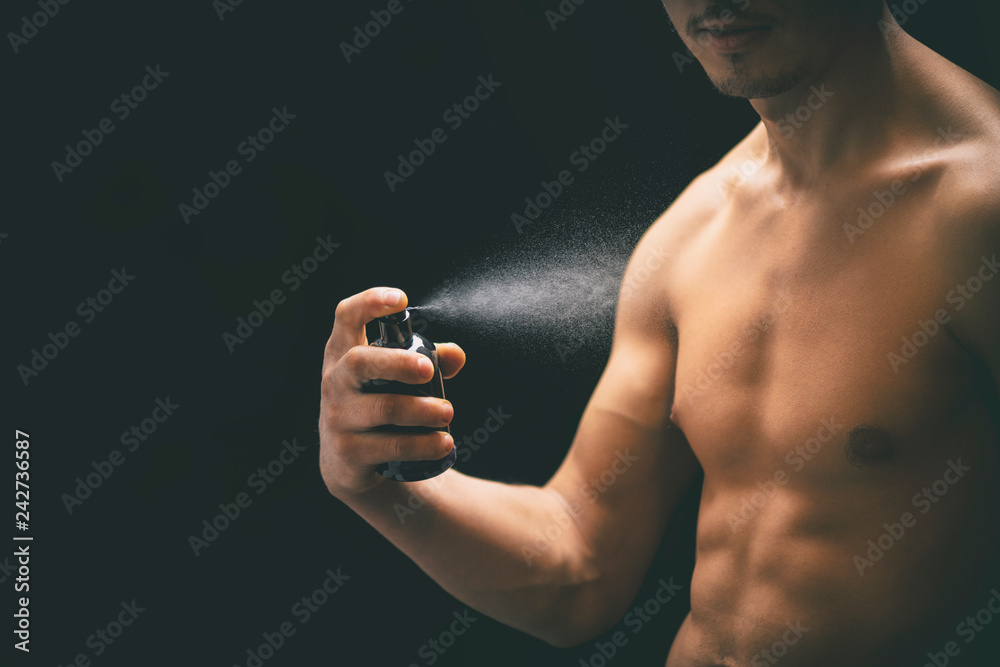 Young man spraying perfume on black background Stock Photo | Adobe Stock