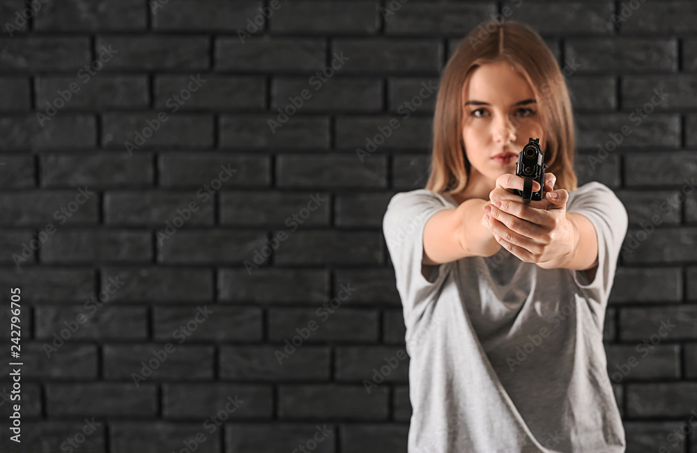 Young woman pointing a gun at viewer against dark brick background ...