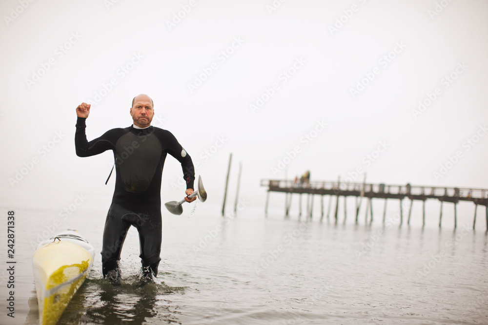 Male kayaker makes a silly face and jumps as he poses with a kayak and ...