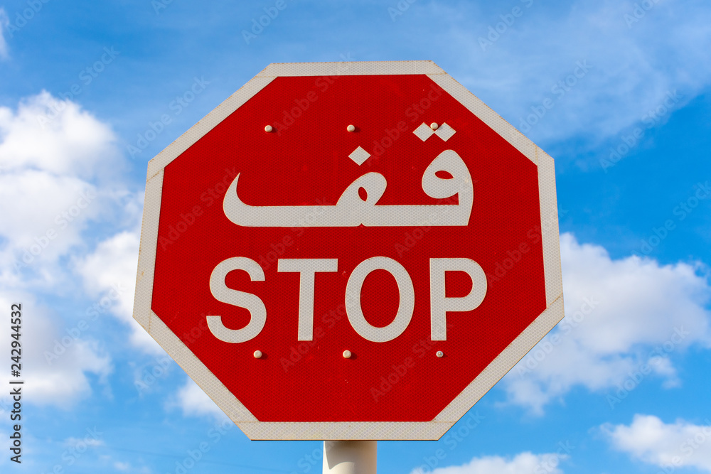 Stop sign in English and Arabic with a blue sky and cloudy background ...