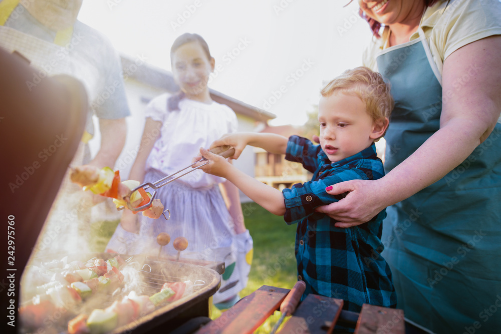 Cute little boy train to turn meat on barbeque grill.Other members of ...