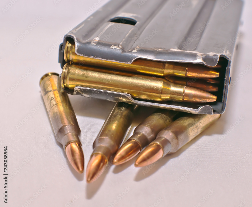 A loaded AR-15 rifle magazine on top of four .223 caliber bullets on a ...