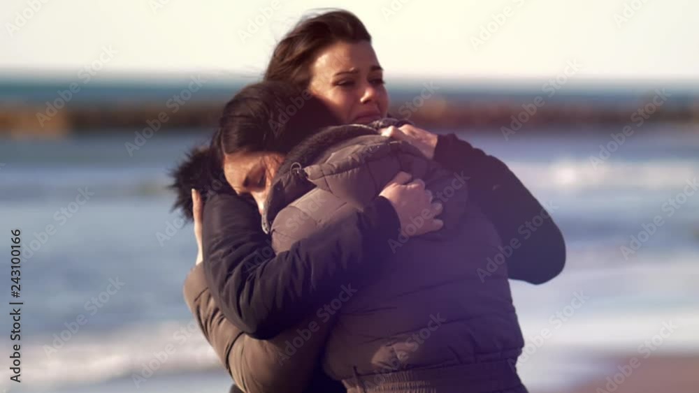 Two sad women hugging crying in front of the ocean slow motion closeup ...