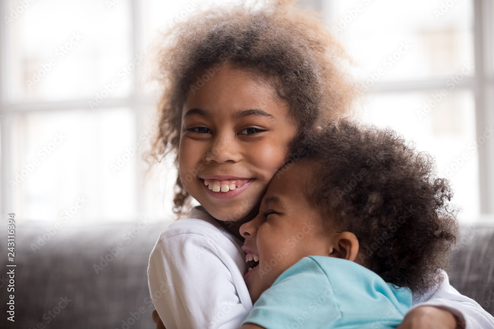 Happy african girl sister embracing little boy brother looking at ...