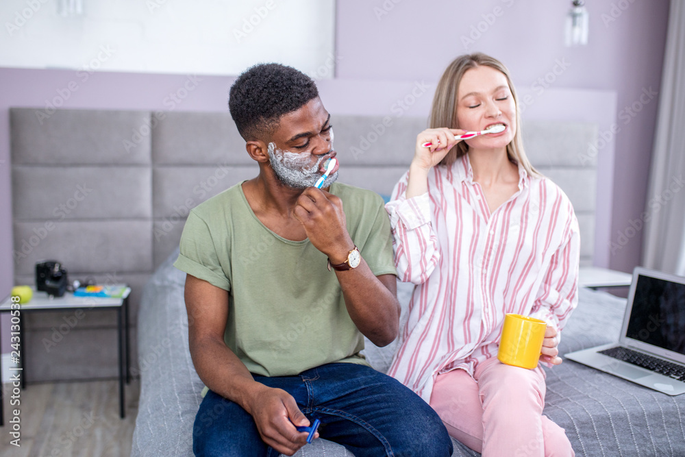 Sleepy young couple in brushing teeth in morning, man is having shaving ...