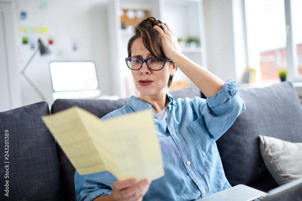 Embarrassed woman tousling her hair while reading travel leaflet at ...