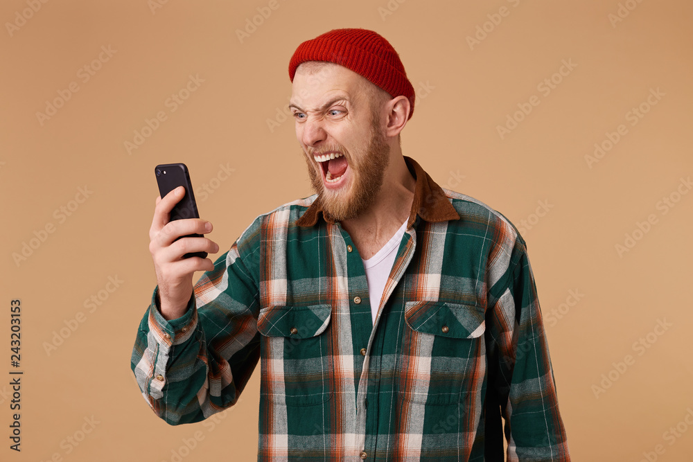 Portrait of angry young man screaming on his mobile phone over beige ...