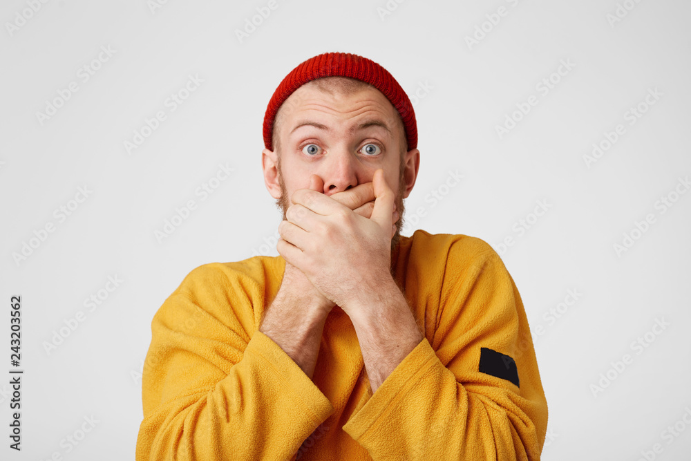 Shocked young man covers his mouth with palms, clamps mouth with hands ...