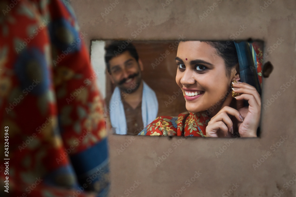 Smiling rural woman looking in the mirror and wearing ear rings with ...