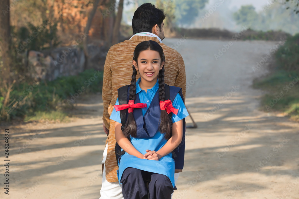 Smiling young school girl riding pillion on bicycle facing backward ...