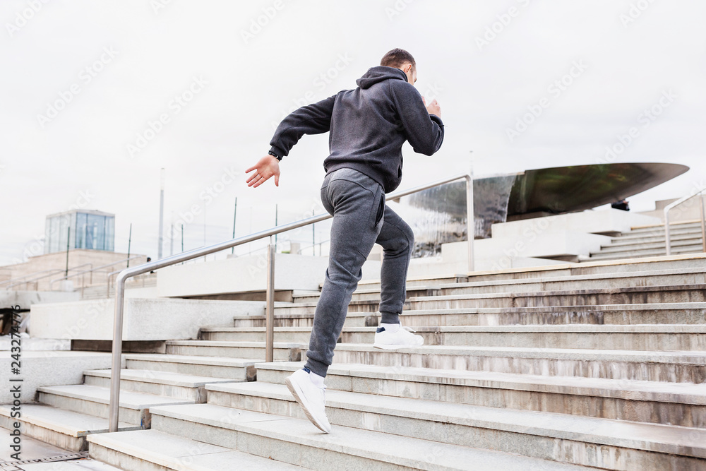 Rear view of a young slim guy a runner in a gray tracksuit and sneakers ...