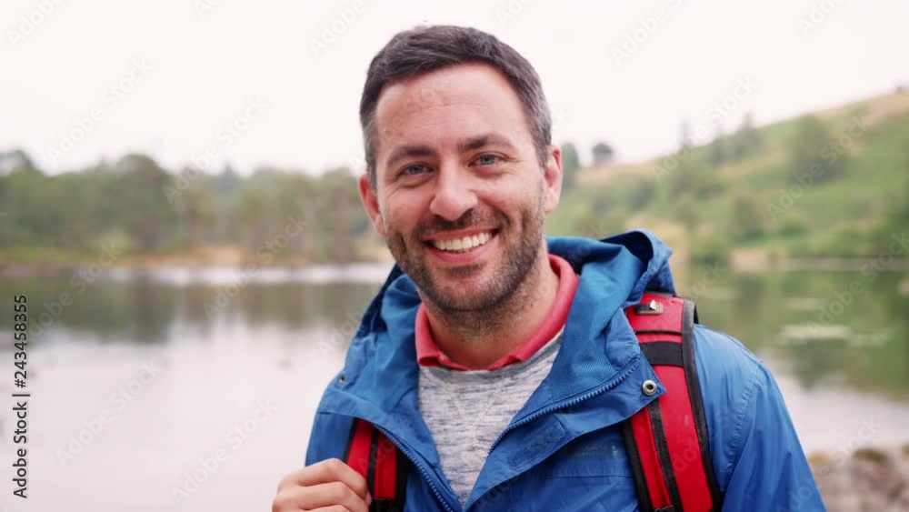 Adult man on a camping holiday standing by a lake smiling, close up ...