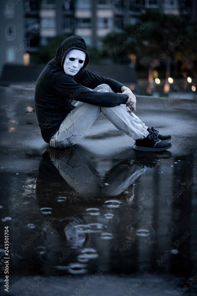 Reflection of mystery hoodie man in white mask hugging his knees ...