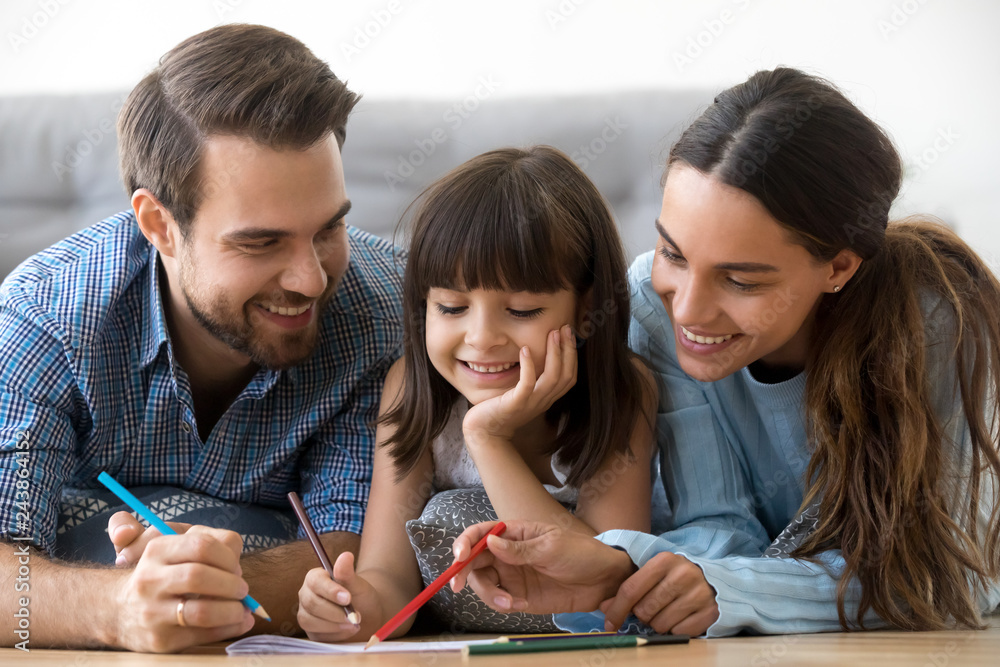 Smiling caring parents and cute little daughter drawing with pencil ...
