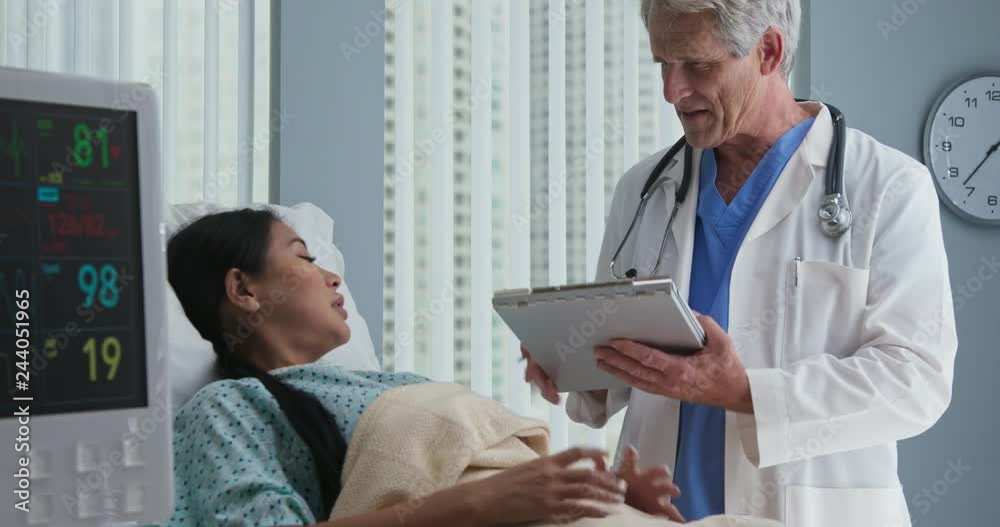 Older male doctor going over chart with female patient lying in ...