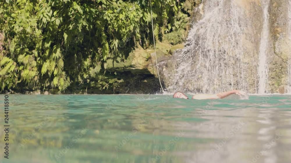 Young woman swimming in blue water of lake from splashing waterfall ...