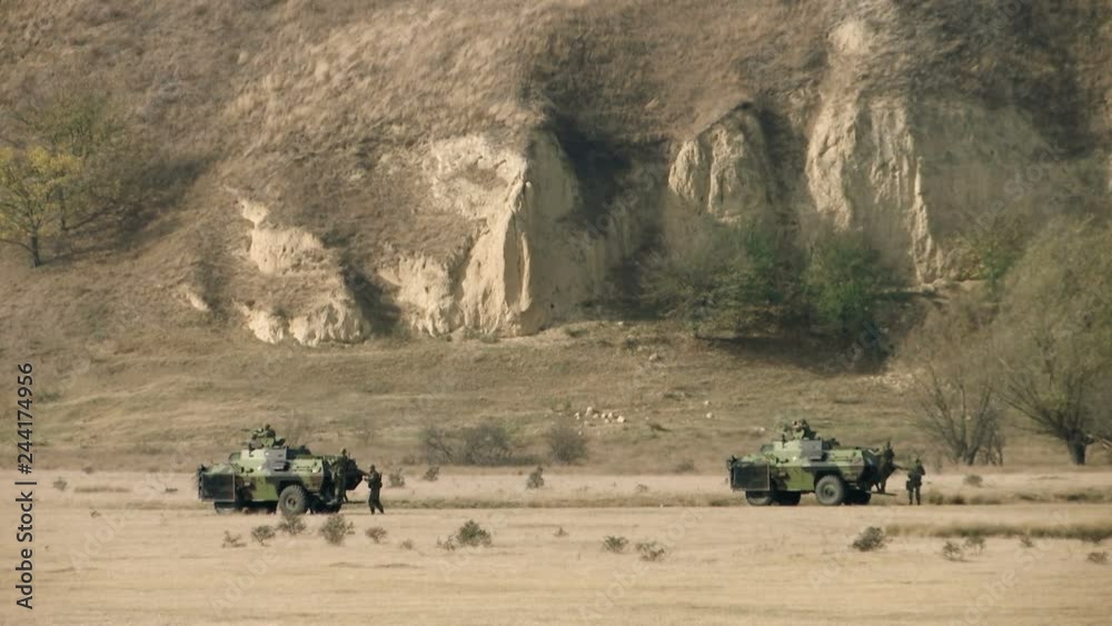 two military combat vehicles in the field under the sand hills with an ...