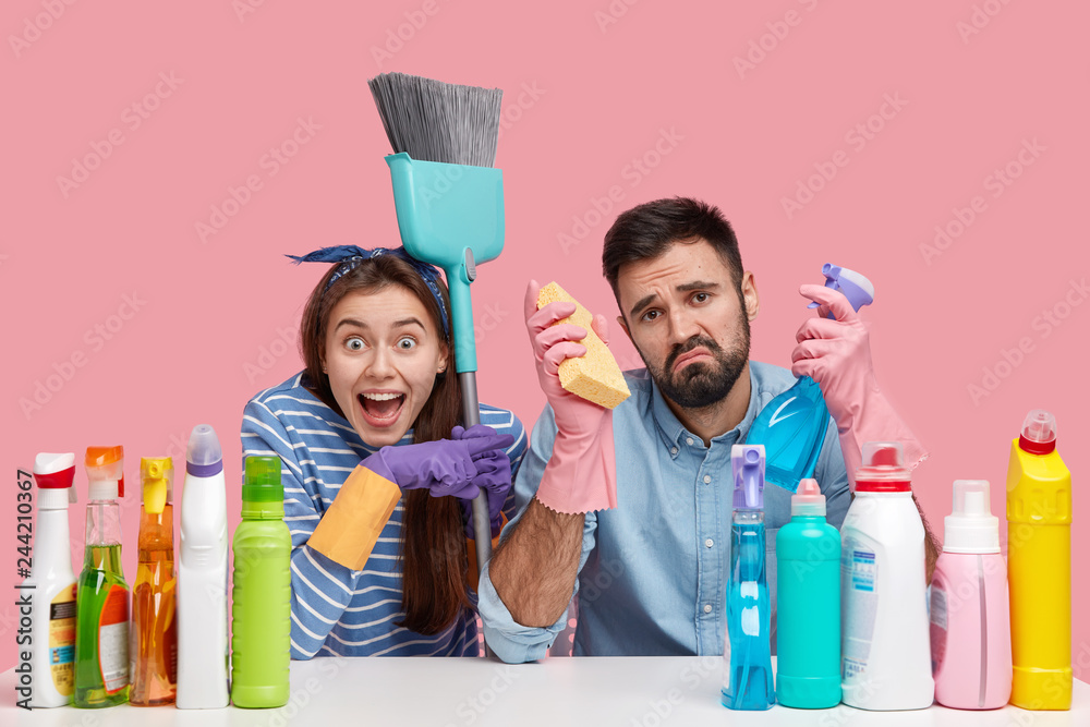 Cleaning concept. Sad young man holds cleanser and sponge, has unhappy ...