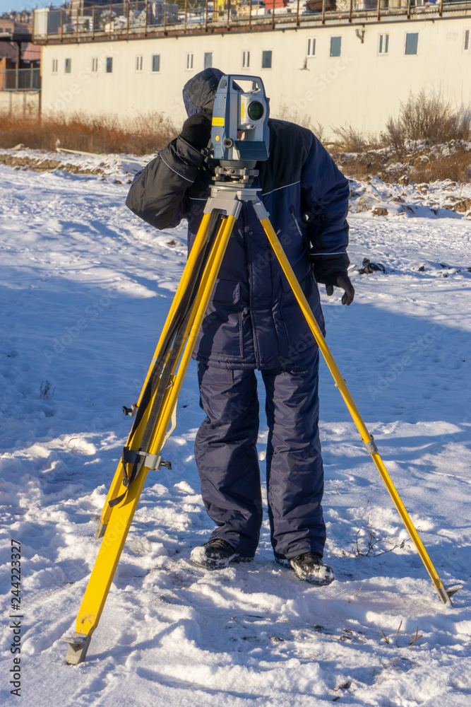 Surveyor in the winter on the construction site conducts topographic ...