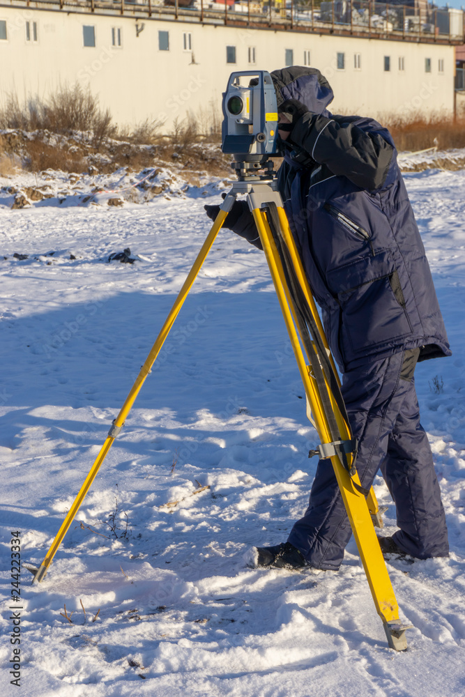 Surveyor in the winter on the construction site conducts topographic ...