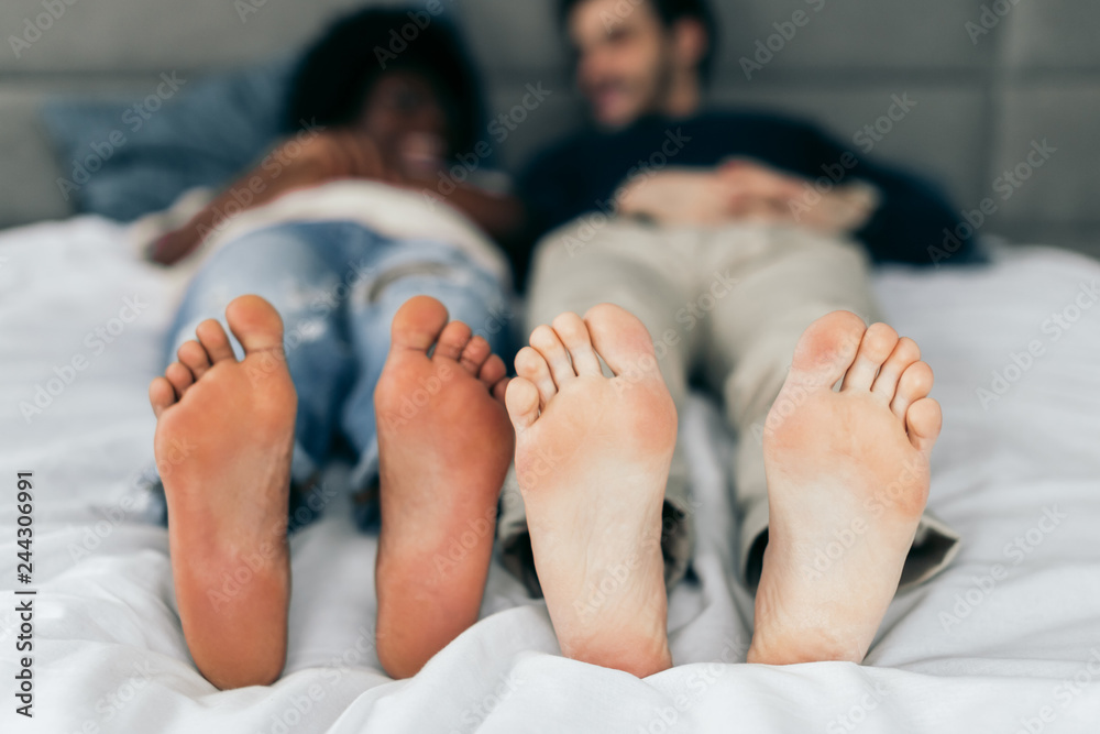 Feet of caucasian man and african woman lying together on bed, casual ...