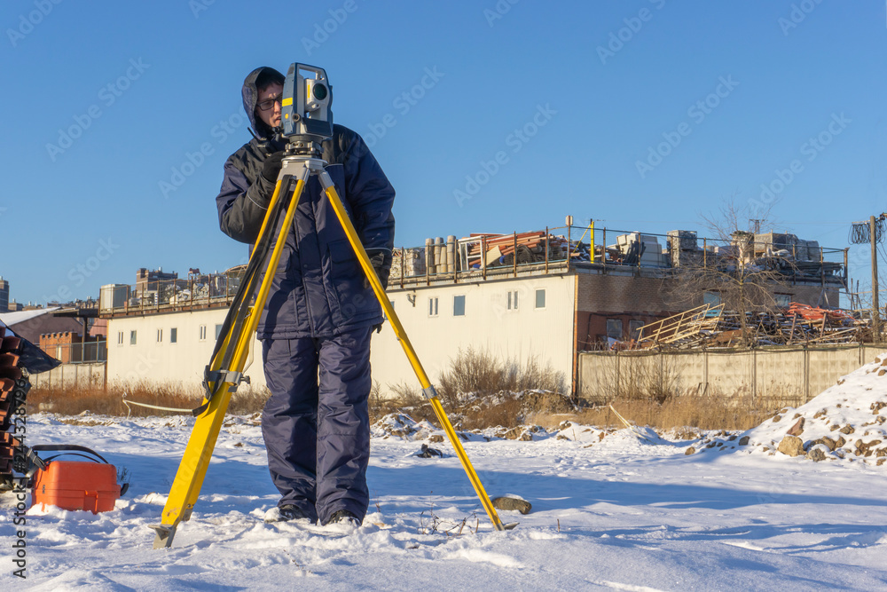 Surveyor in the winter on the construction site conducts topographic ...