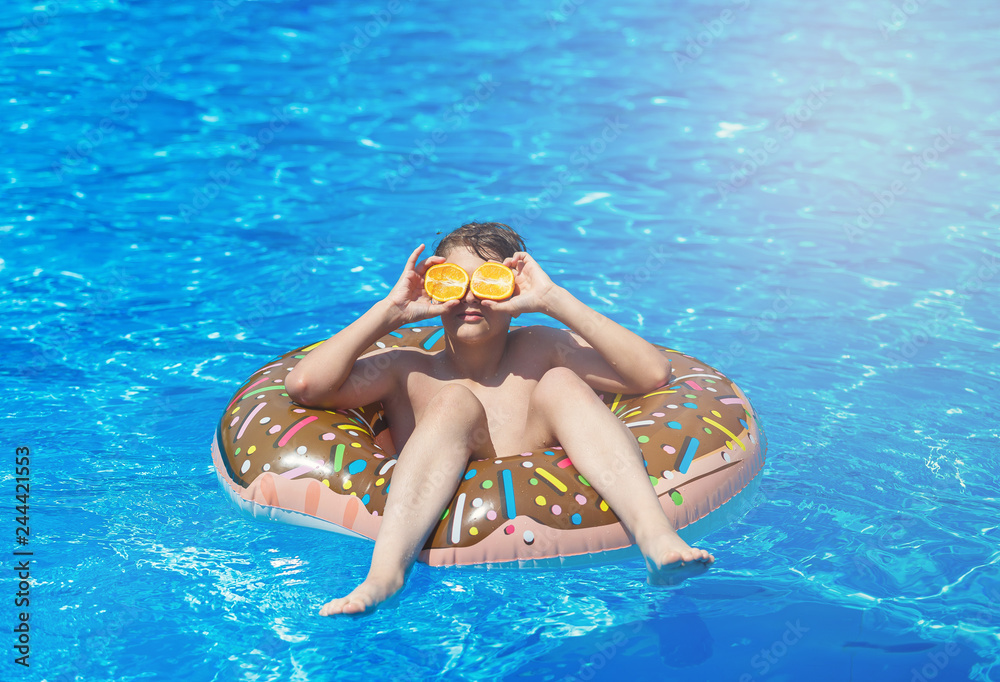Cute child boy on funny inflatable donut float ring in swimming pool with oranges. Teenager ...