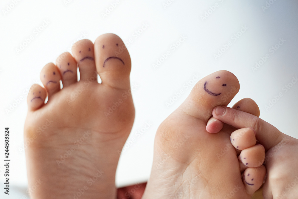 Female toes with painted smileys and children's hands. Foot care ...