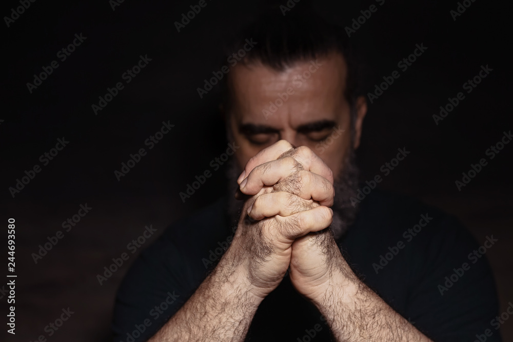 Man bowing his head in prayer with clasped hands in front of his face ...