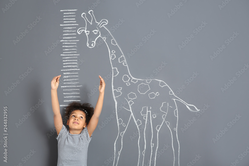 African-American child measuring height near chalk giraffe drawing on ...