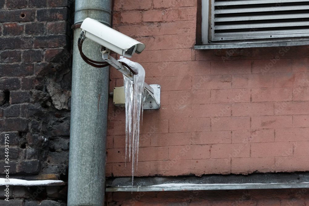 CCTV Camera covered with ice and icicles against brick wall,turned ...